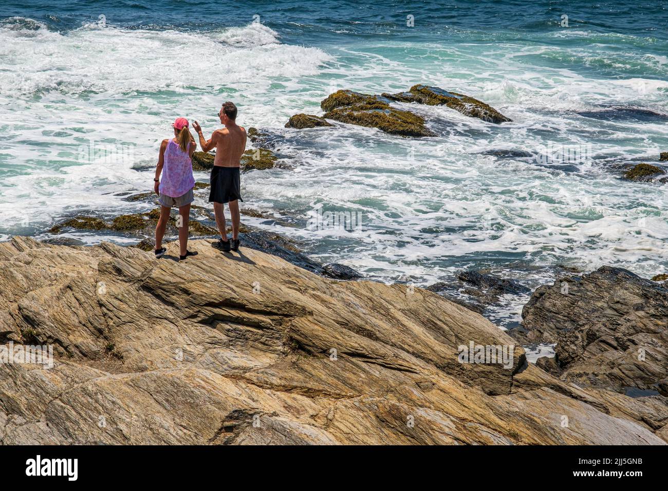 Couple standing on the rocks at the ocean's edge in Beaver Tail State ...