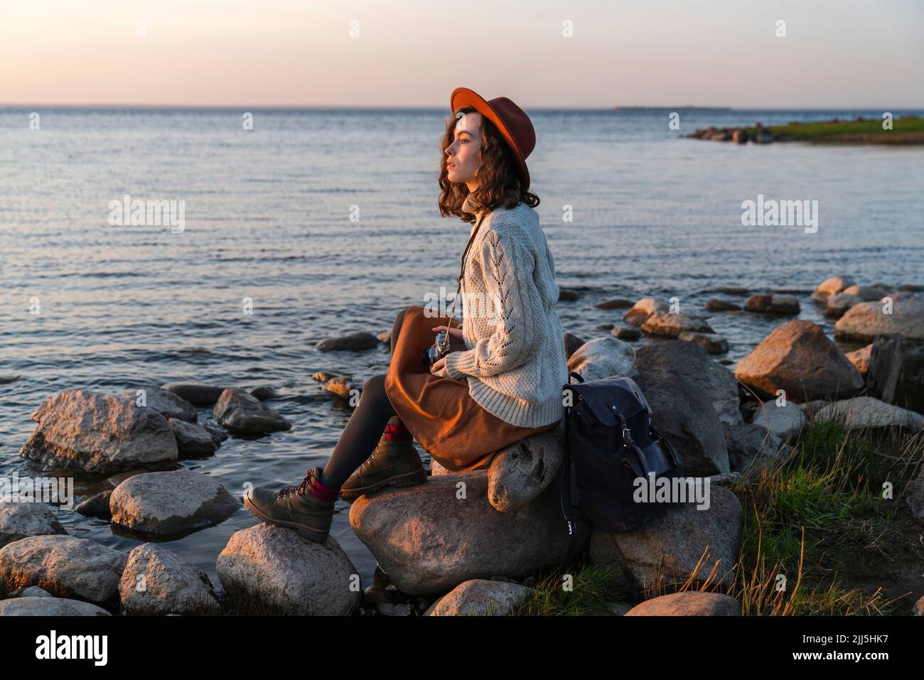 Young woman wearing hat sitting on rock at sea coast Stock Photo - Alamy