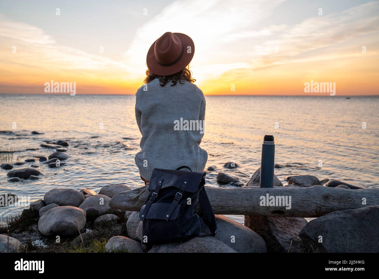 Young woman with backpack sitting on log at sunset Stock Photo - Alamy