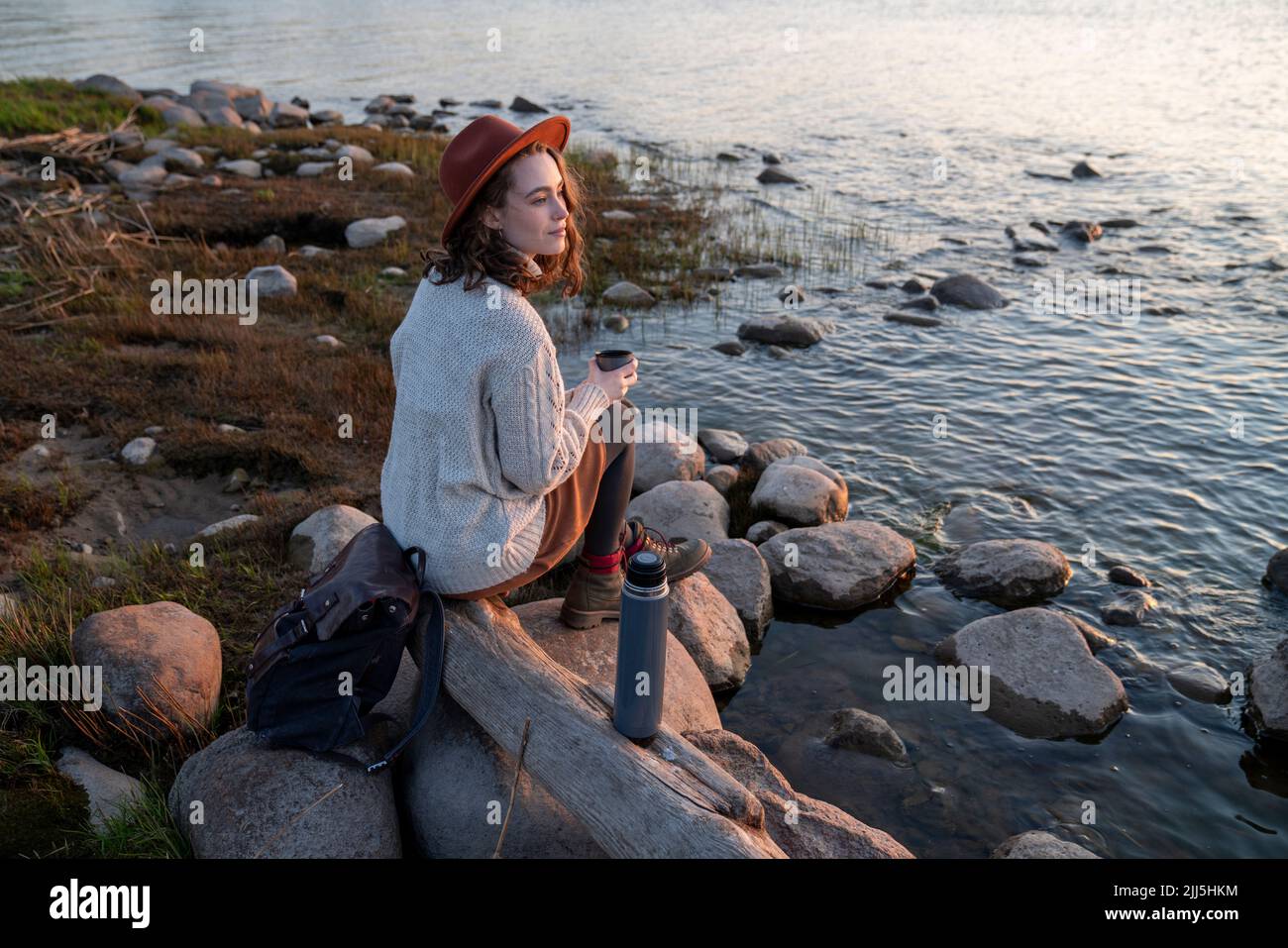 Smiling woman sitting on log by water Stock Photo - Alamy