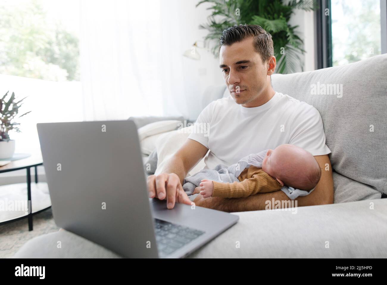 Man carrying baby in arm working from home Stock Photo - Alamy