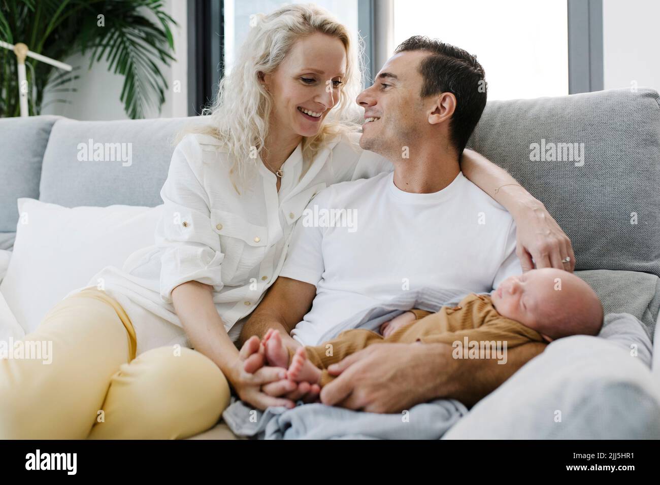 Man carrying baby in arm sitting by woman on sofa at home Stock Photo ...
