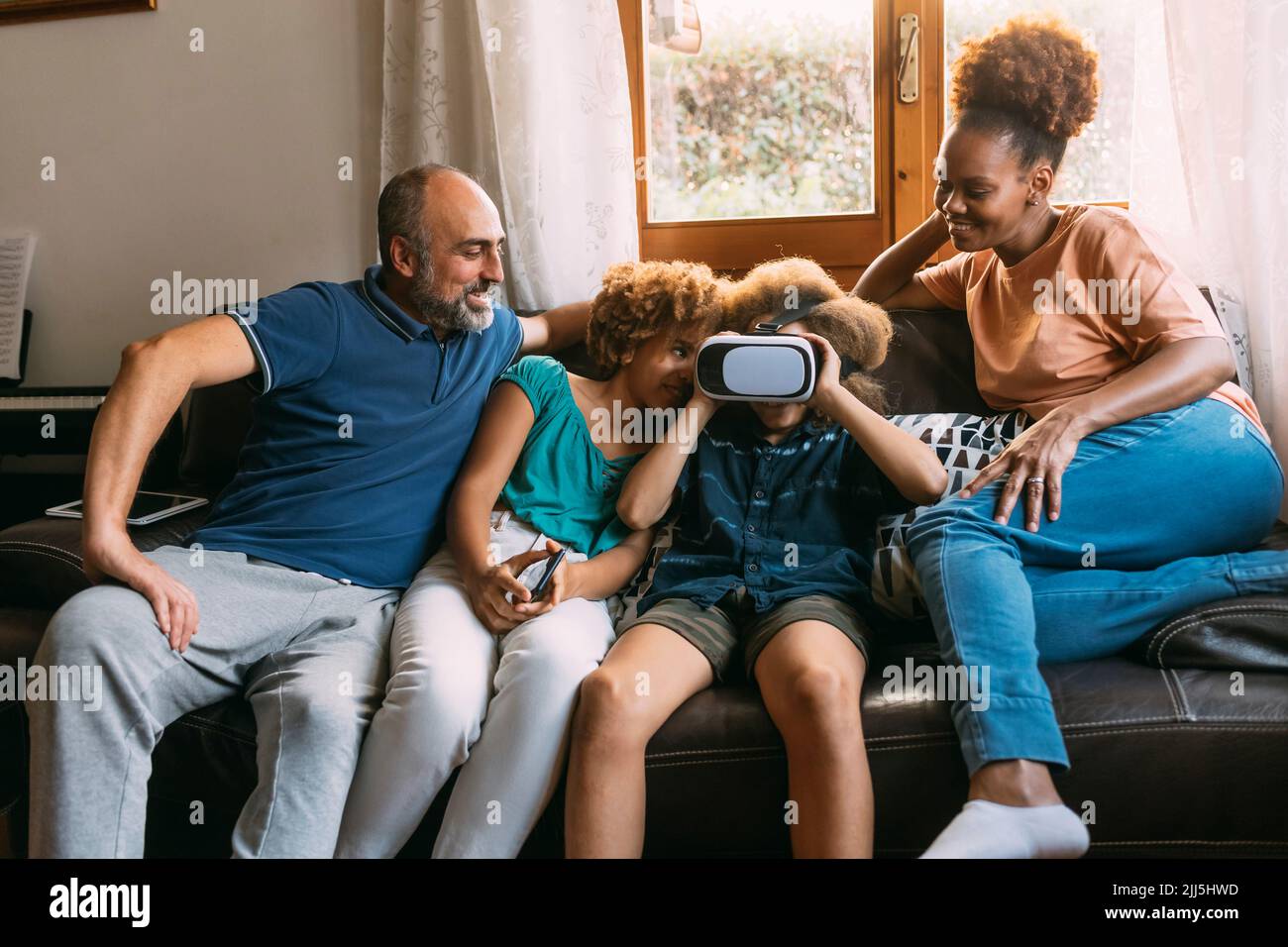 Boy wearing virtual reality simulator sitting by sister and parents on ...