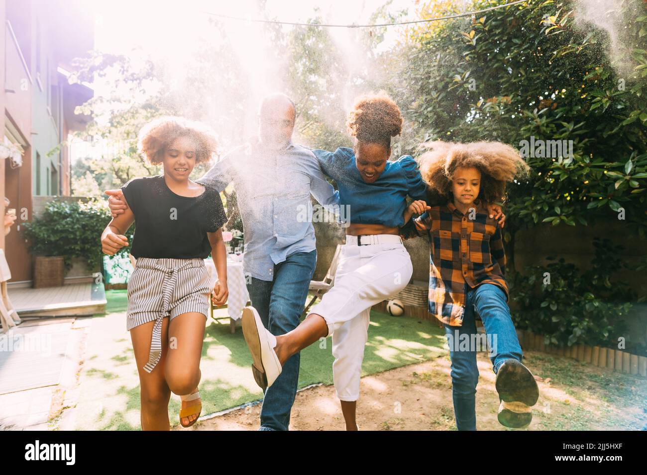 Happy woman with family dancing under splashing water in backyard Stock ...