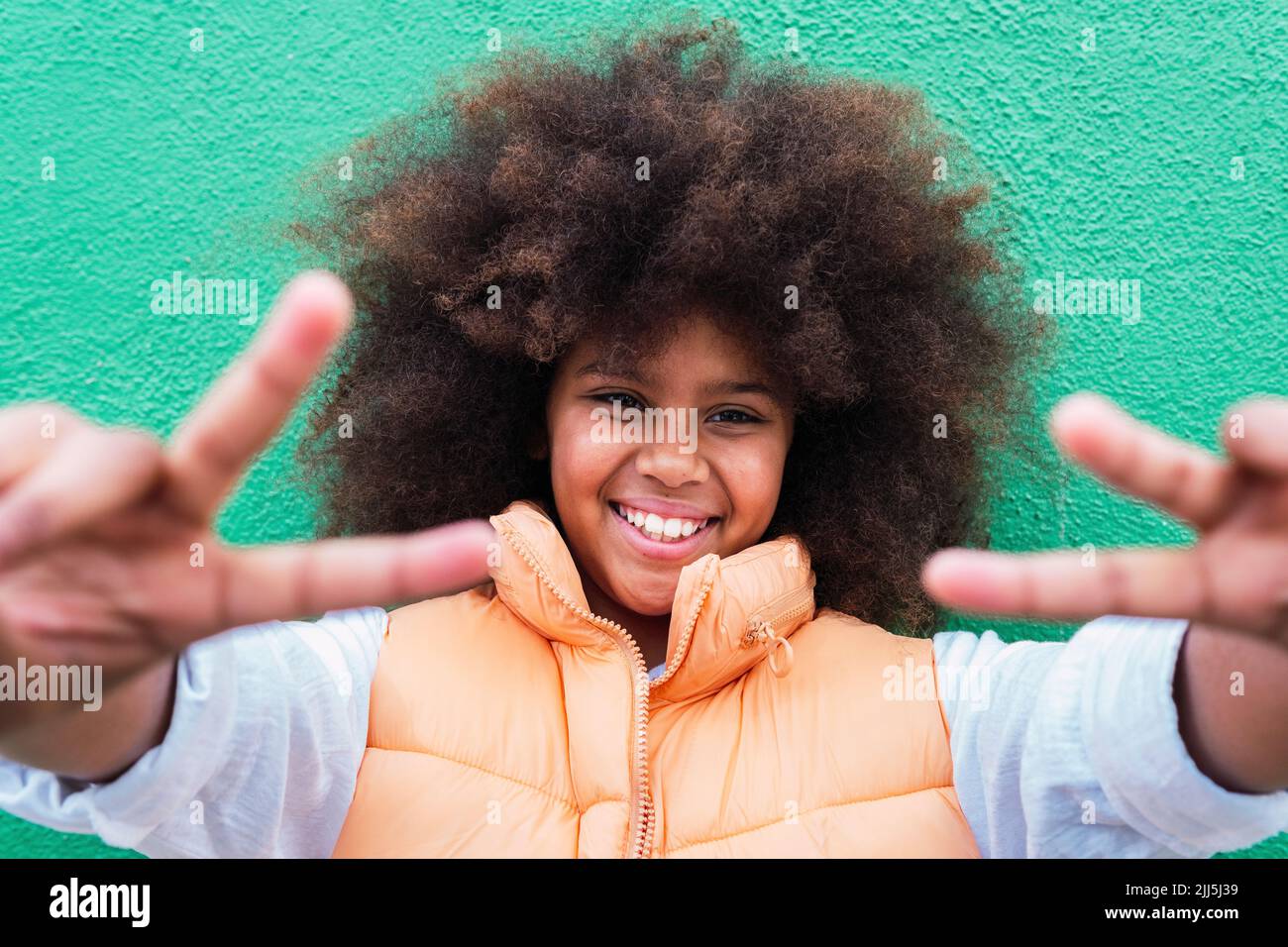 Smiling girl gesturing peace sign in front of wall Stock Photo - Alamy