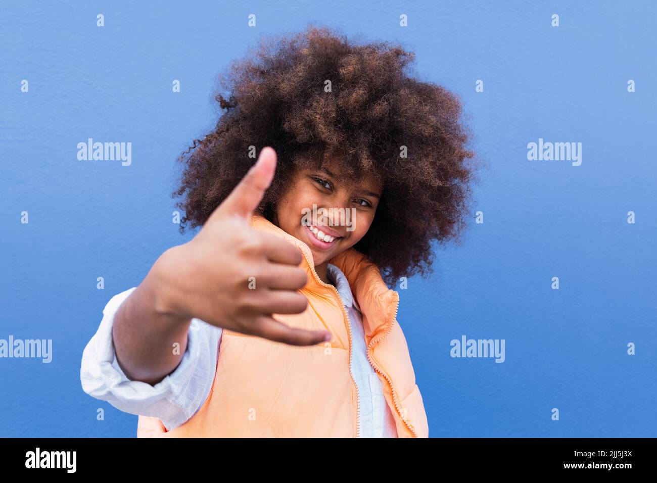 Smiling girl gesturing shaka sign against blue background Stock Photo ...