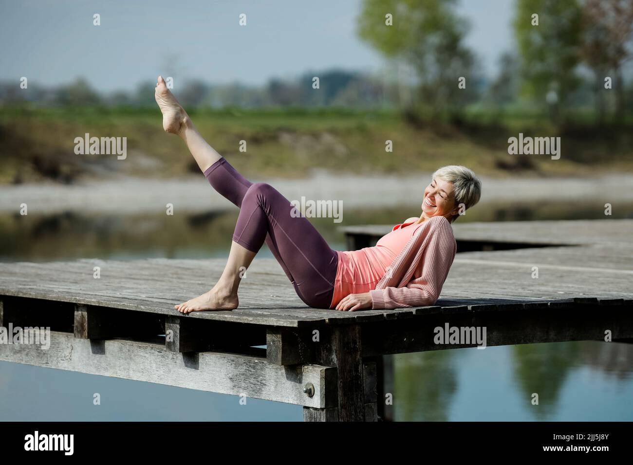 Happy woman with foot up lying on pier Stock Photo - Alamy