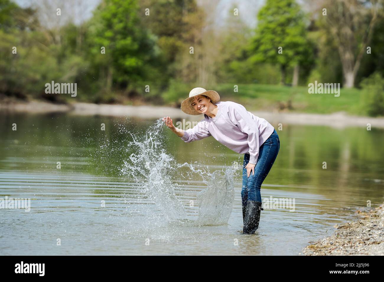 Happy woman wearing hat splashing water at lake Stock Photo - Alamy