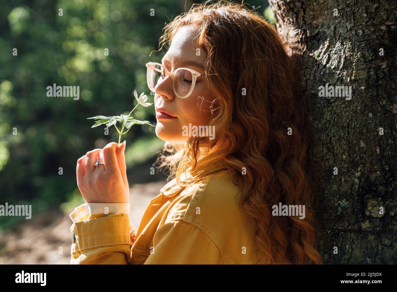 Woman with eyes closed smelling small flower in forest Stock Photo - Alamy