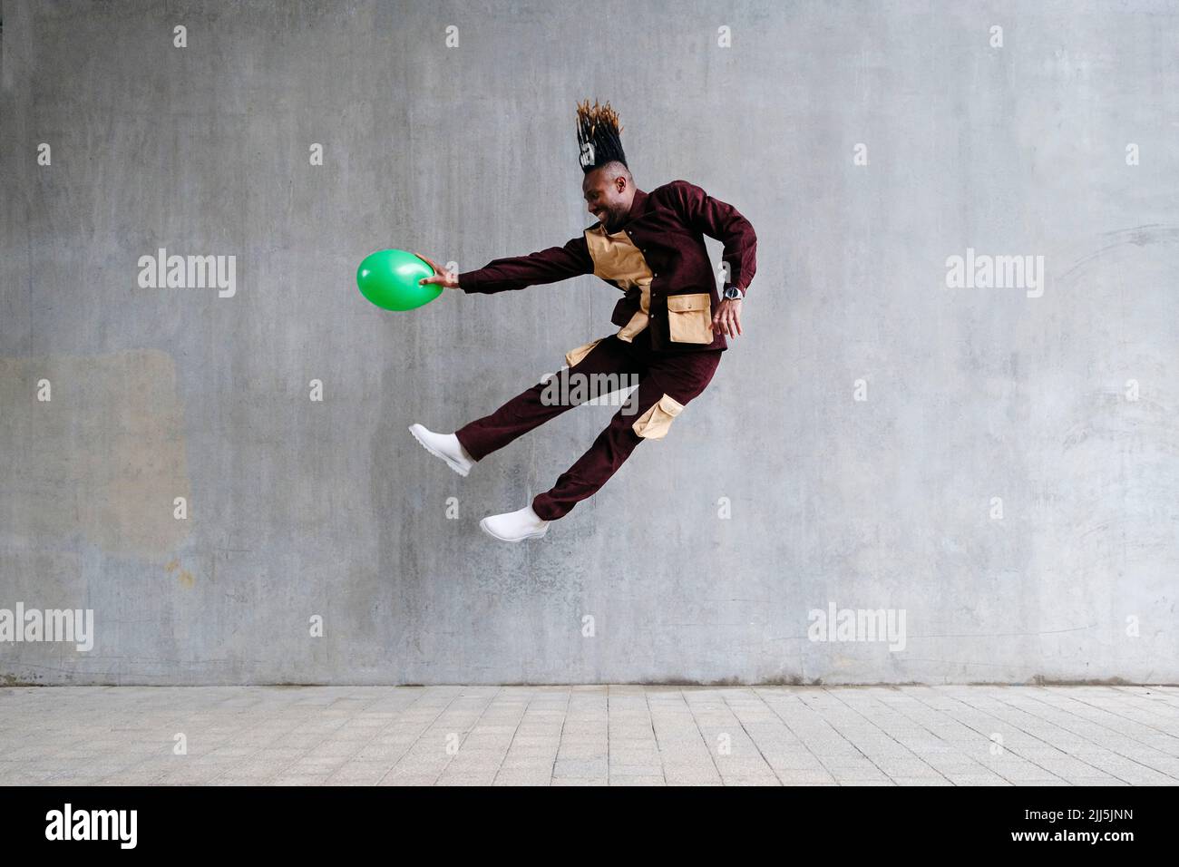 Playful man with balloon jumping in front of concrete wall Stock Photo ...