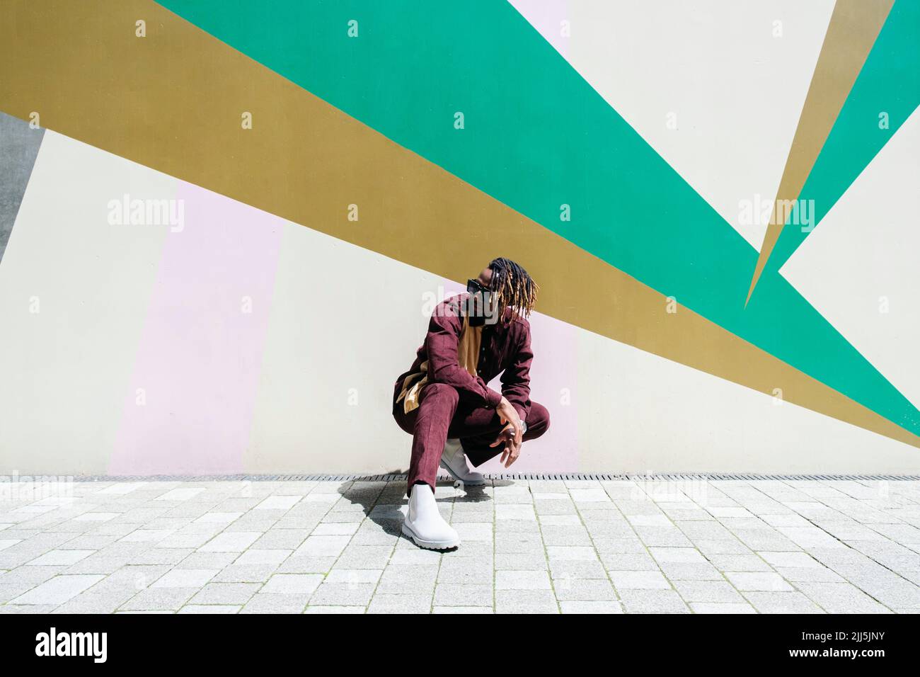 Man crouching in front of colorful wall Stock Photo - Alamy
