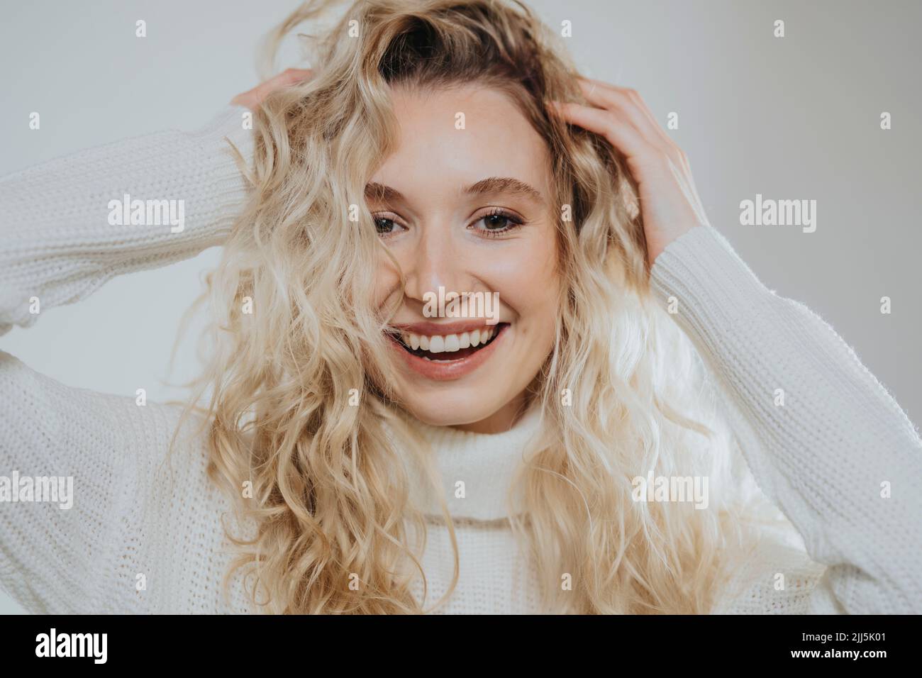 Happy blond woman with hand in hair against white background Stock Photo - Alamy
