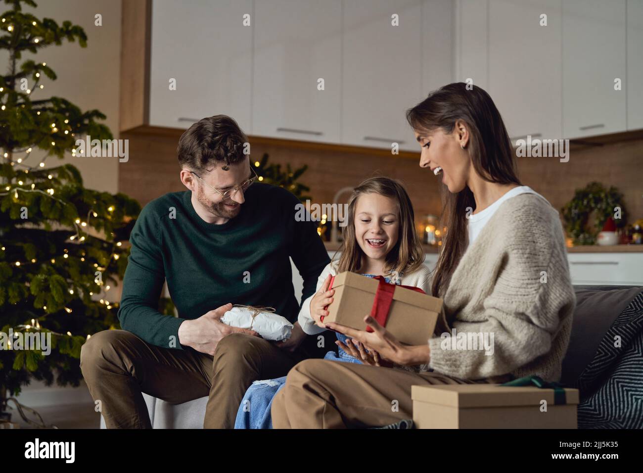 Happy parents giving Christmas gift to daughter sitting on sofa Stock ...