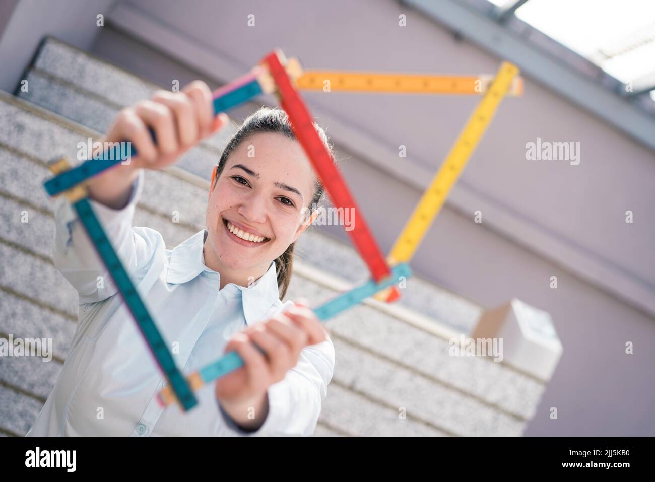 Young female architect making house shape with folding ruler at factory ...