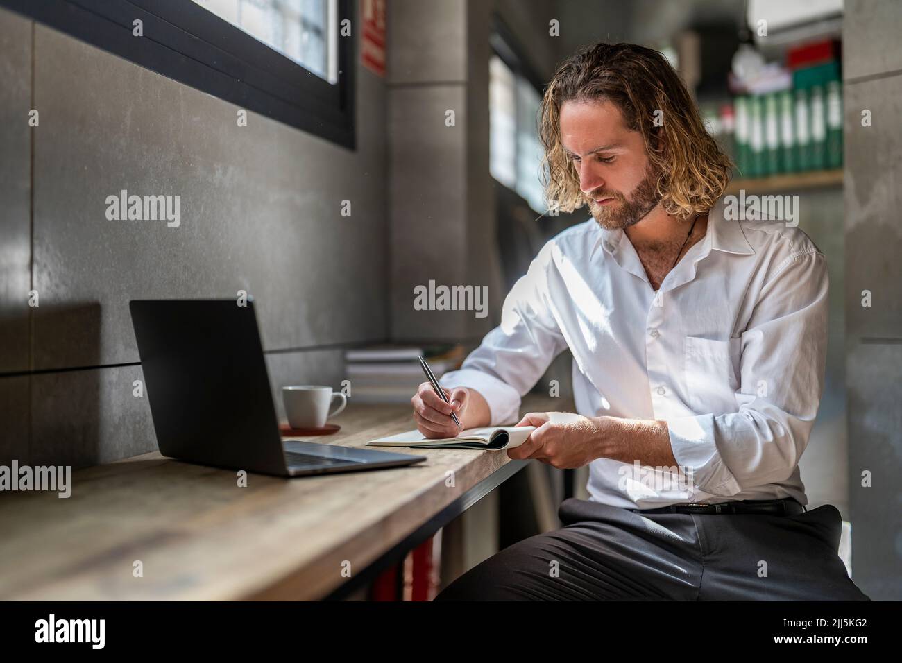 Executive writing in diary sitting with laptop on table at office Stock ...