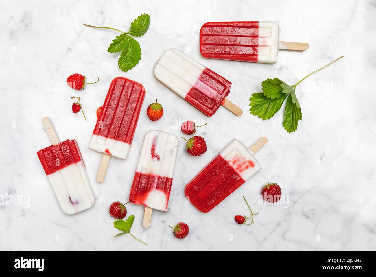 Homemade strawberry-yogurt popsicles flat laid against white marble ...