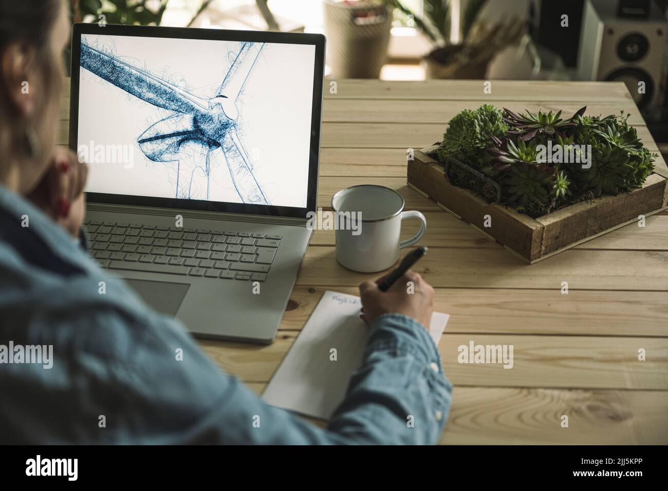 Freelancer writing notes with wind turbine sketch on laptop screen at ...