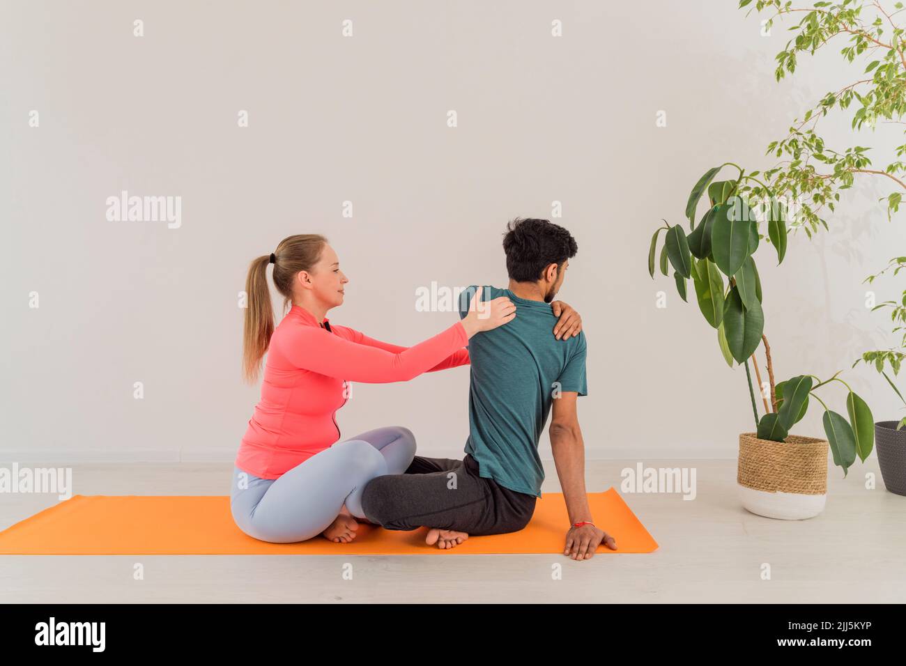 Instructor helping man with stretching exercise at yoga class Stock ...