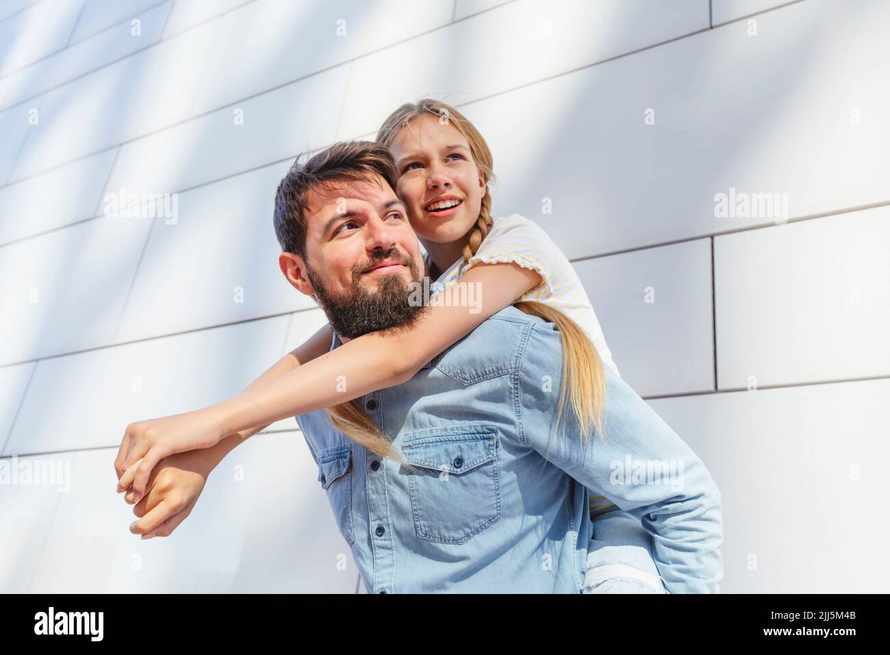 Smiling man giving piggyback ride to daughter in front of wall Stock ...