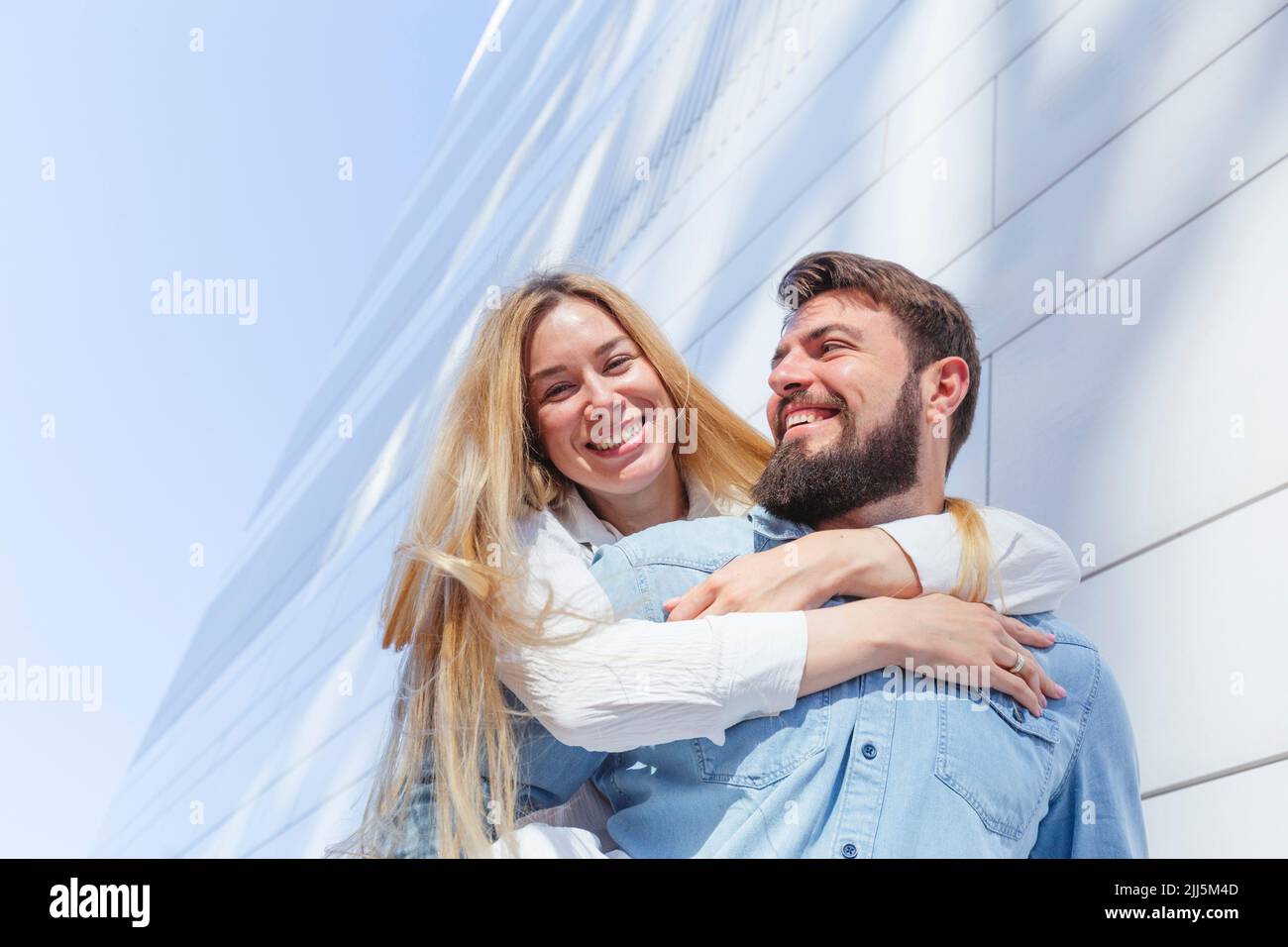 Happy man giving piggyback ride to woman in front of wall Stock Photo ...
