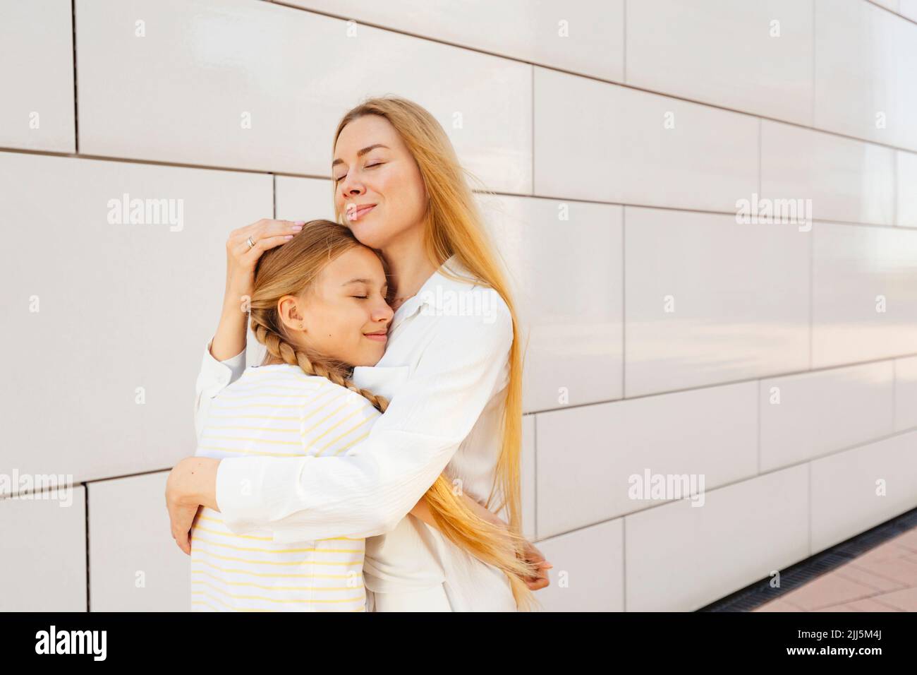 Happy mother hugging daughter in front of wall Stock Photo - Alamy