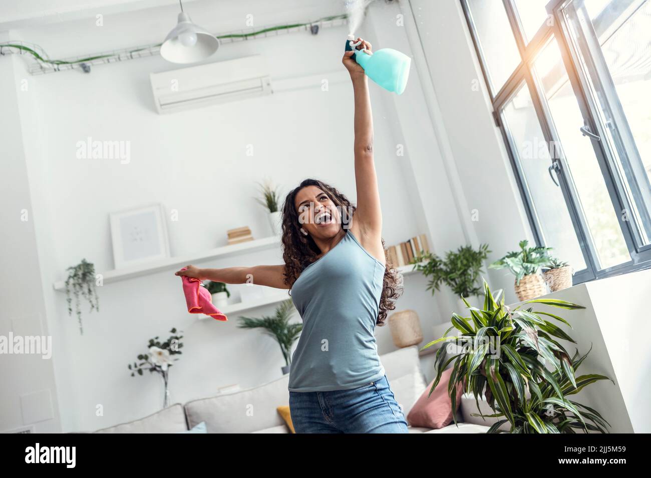 Happy woman cleaning home spraying water from bottle Stock Photo - Alamy