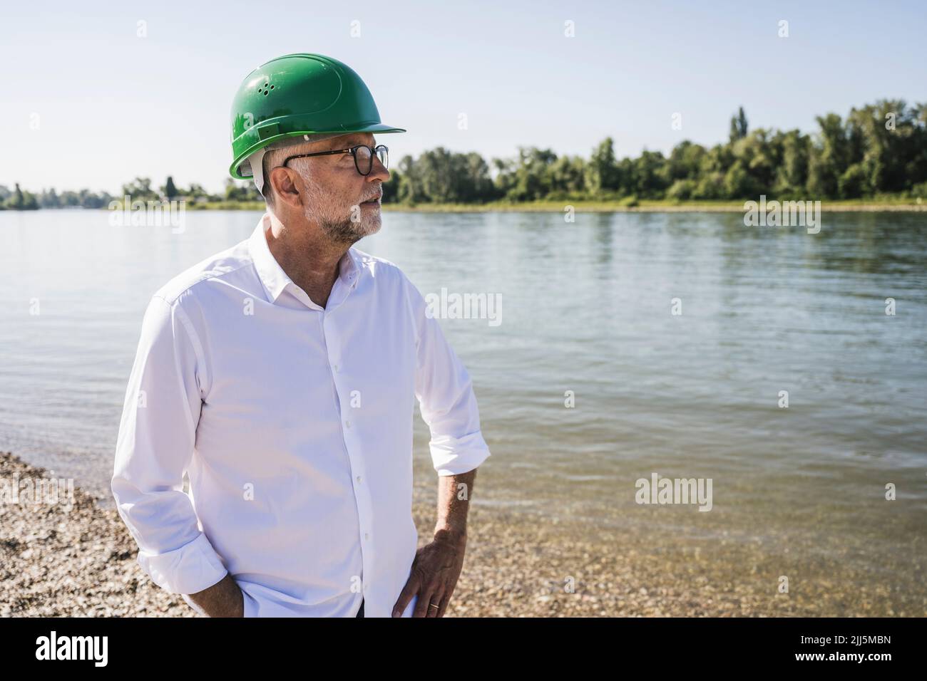 Engineer wearing green hardhat standing at riverbank Stock Photo - Alamy