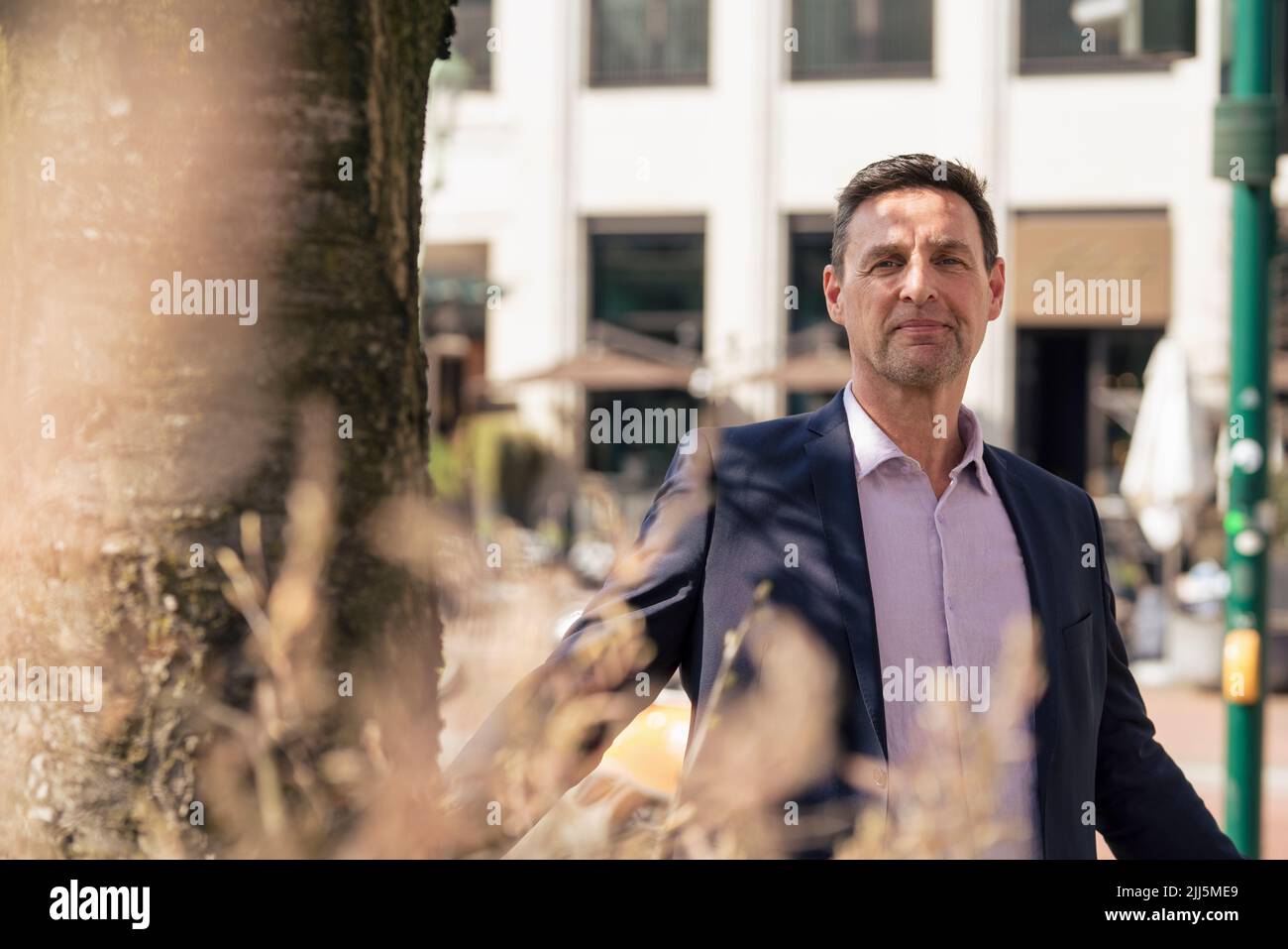 Smiling businessman standing near tree trunk Stock Photo - Alamy
