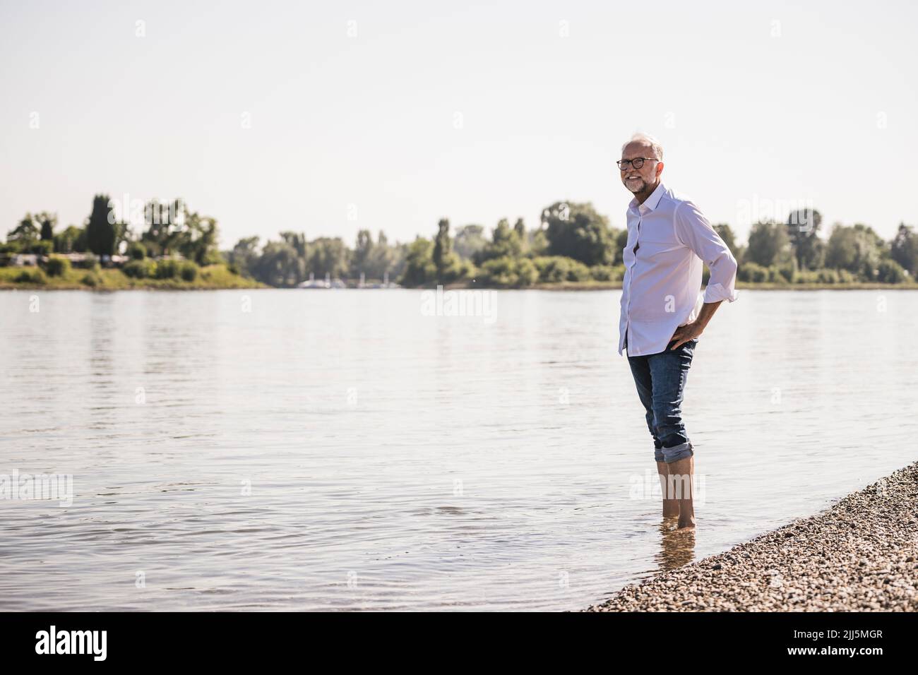 Smiling man standing with hand on hip at riverbank Stock Photo - Alamy