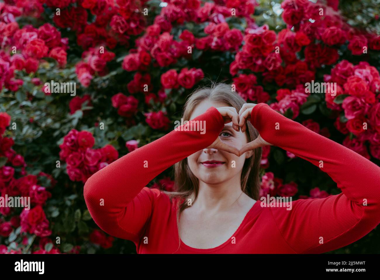 Woman gesturing heart shape in front of rose bush Stock Photo - Alamy