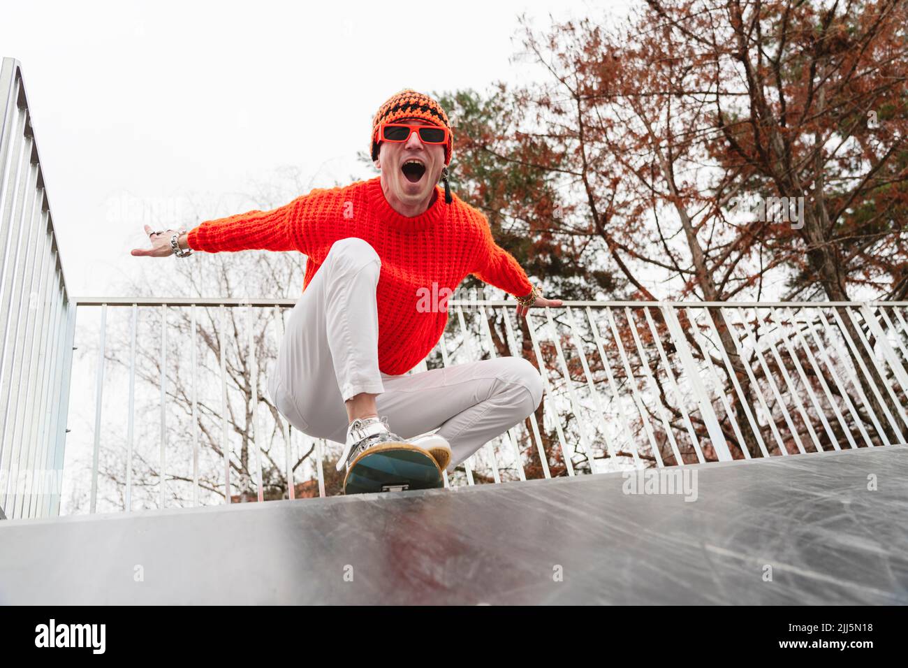 Happy man with arms outstretched squatting on skateboard in front of ...