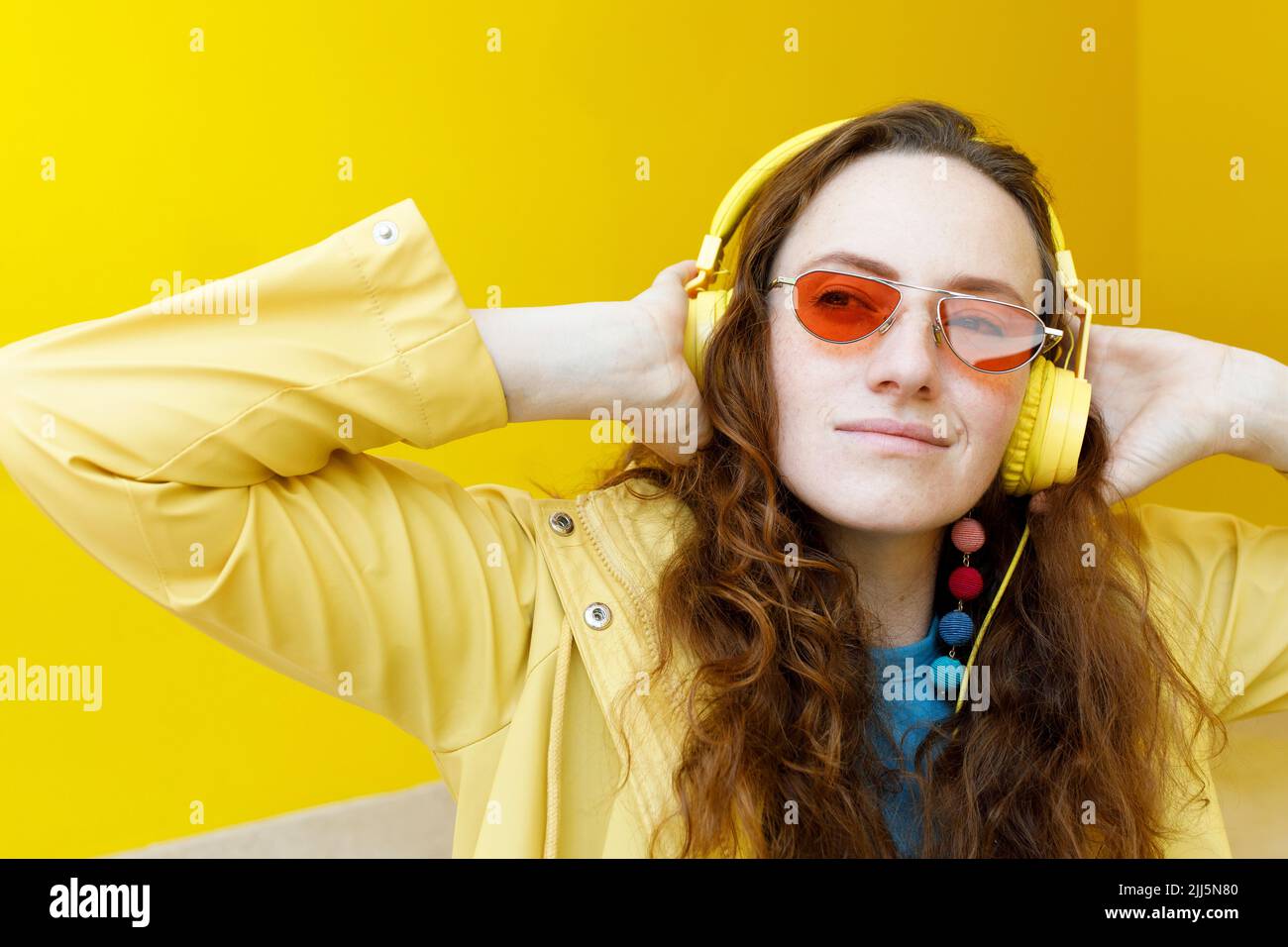 Woman in yellow raincoat listening music through headphone in front of ...