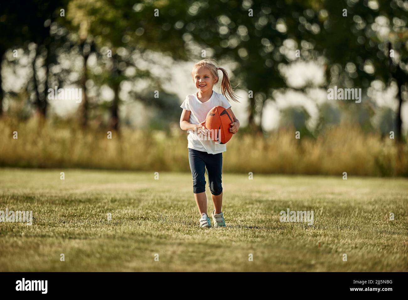 Smiling girl with rugby ball walking at sports field Stock Photo - Alamy