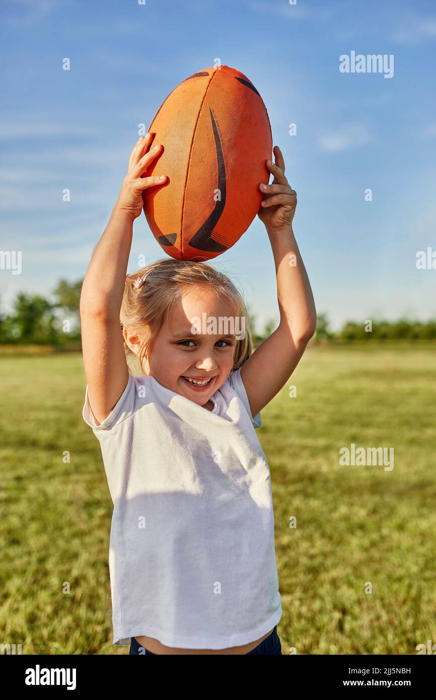 Happy blond girl carrying rugby ball on head at sports field Stock ...