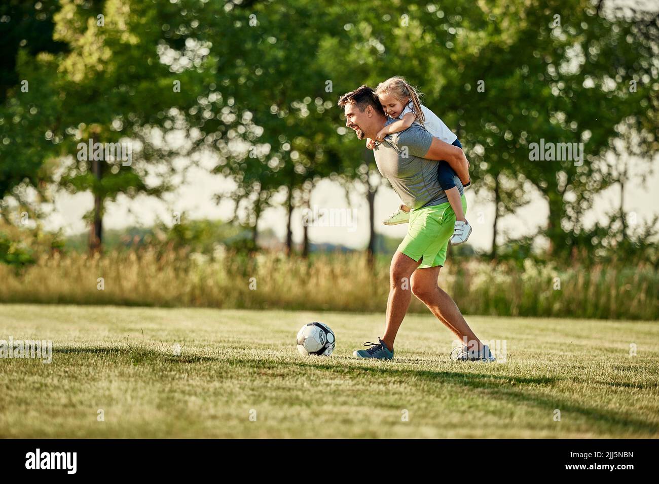 Happy girl enjoying piggyback ride given by man playing soccer at ...