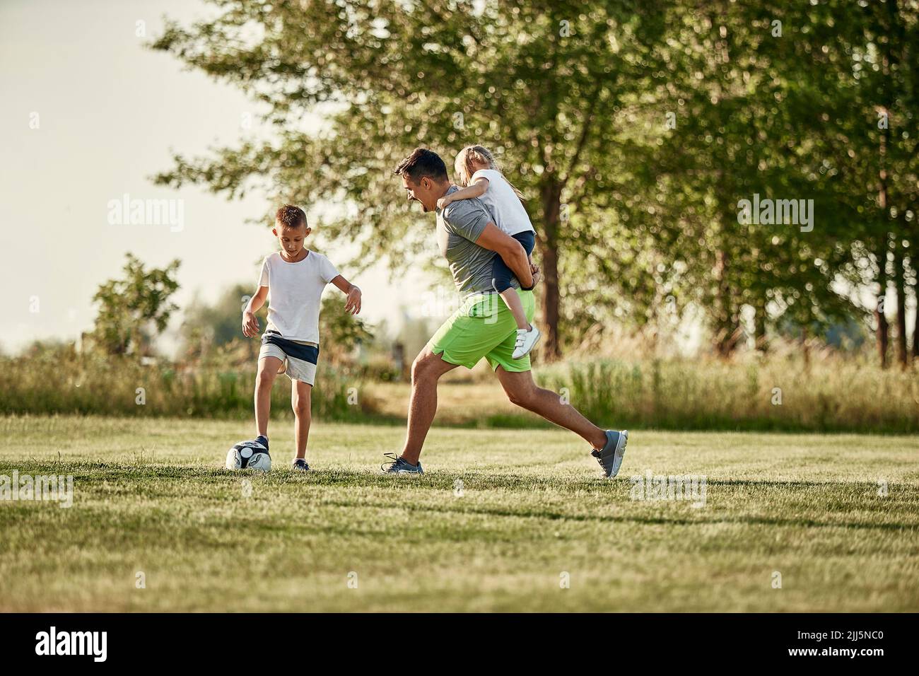 Man giving piggyback ride to daughter by son playing soccer at sports ...