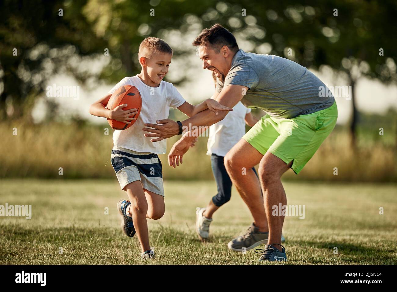Cheerful man chasing son running with rugby ball at sports field Stock ...