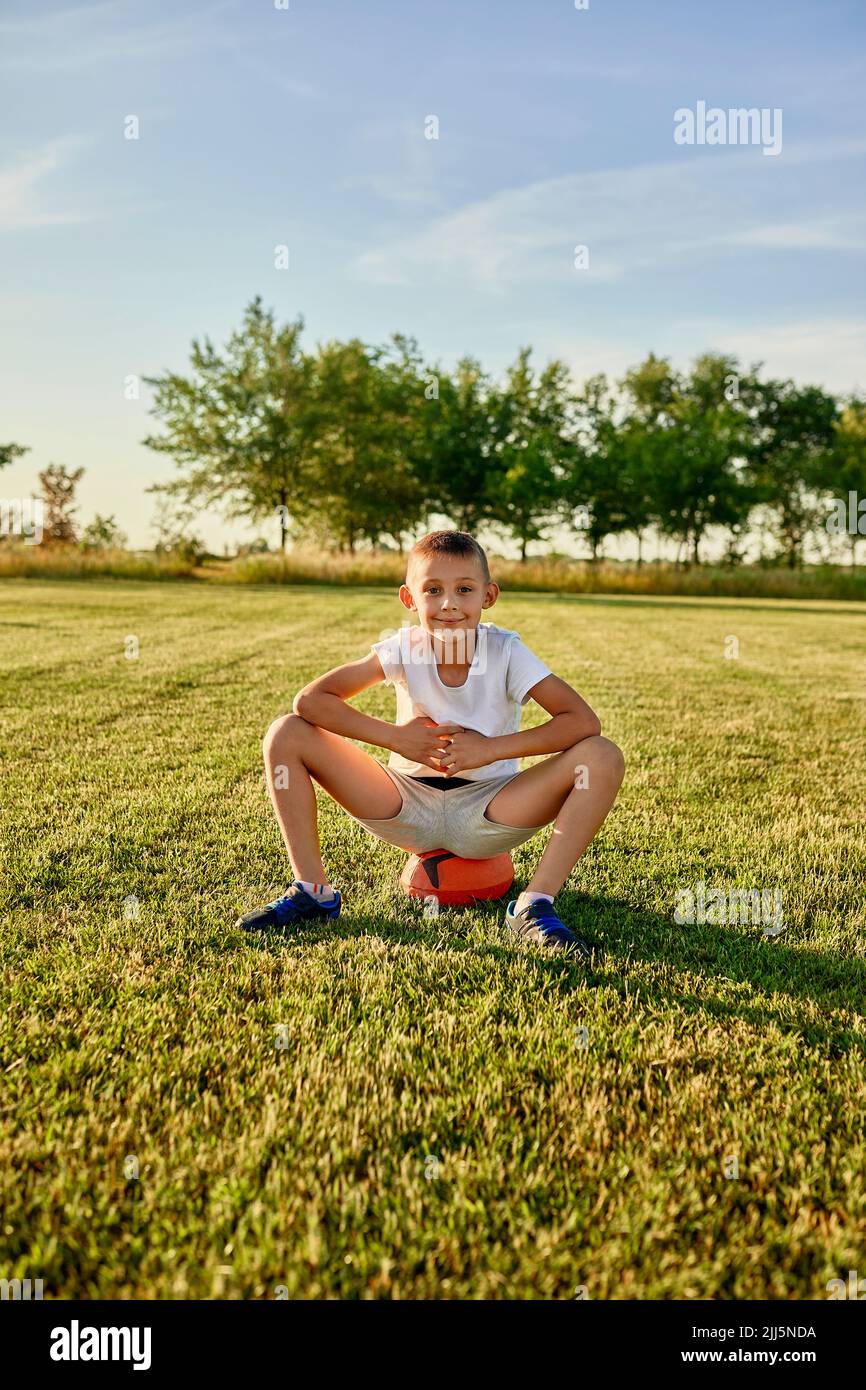 Smiling boy sitting on rugby ball at sports field Stock Photo - Alamy