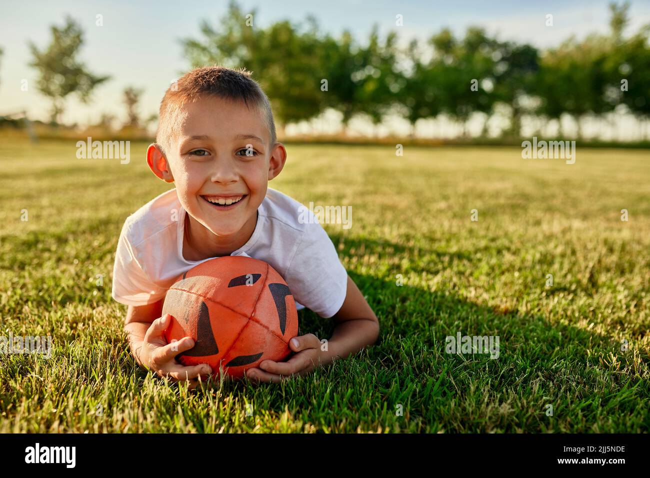 Happy boy with rugby ball lying at sports field on sunny day Stock ...