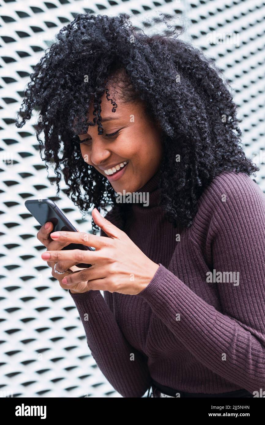 Happy woman text messaging through smart phone in front of wall Stock ...