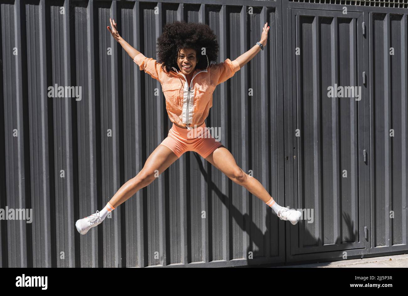 Cheerful Afro sports woman jumping in front of black wall Stock Photo - Alamy