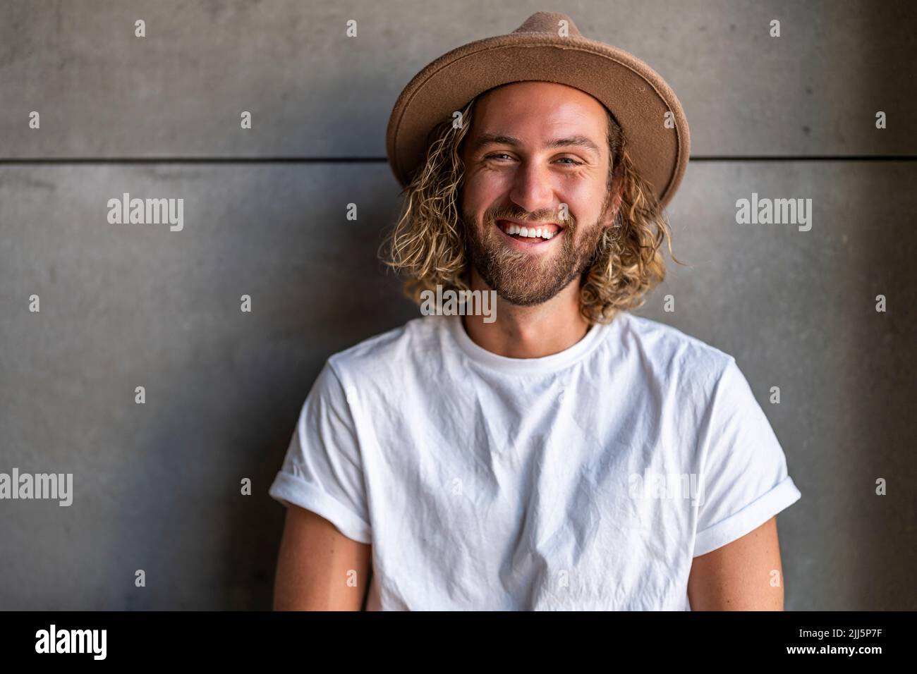Happy man wearing hat in front of wall Stock Photo - Alamy