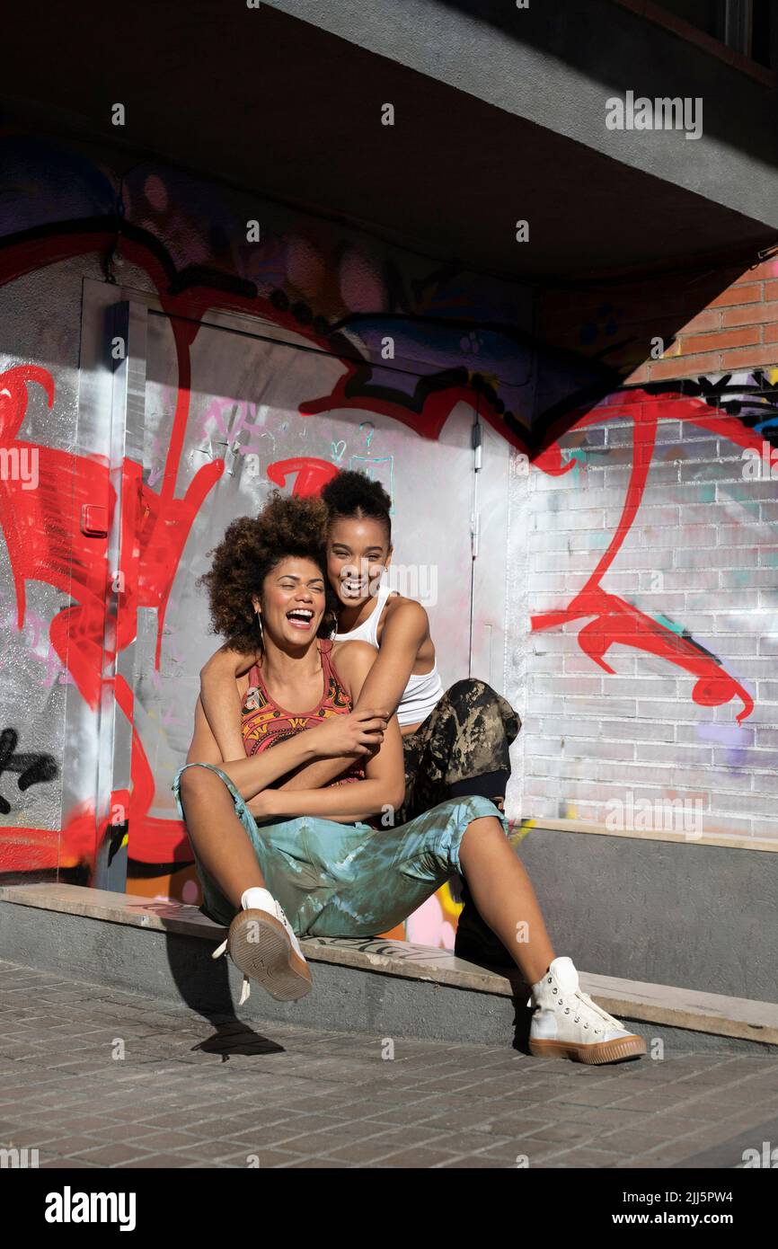 Happy friends embracing in front of graffiti wall on sunny day Stock ...