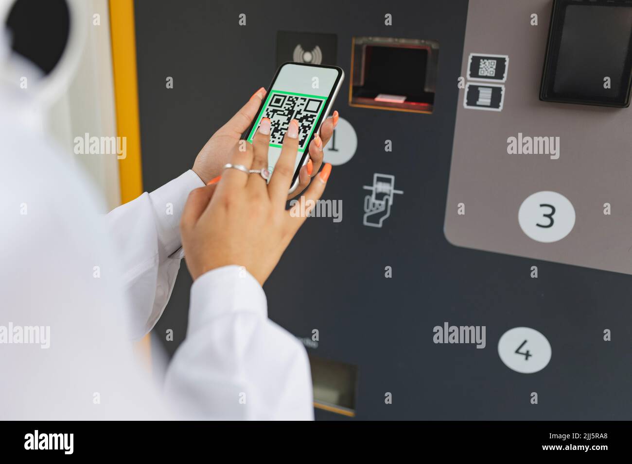 Woman scanning QR code through smart phone near ticket vending machine ...
