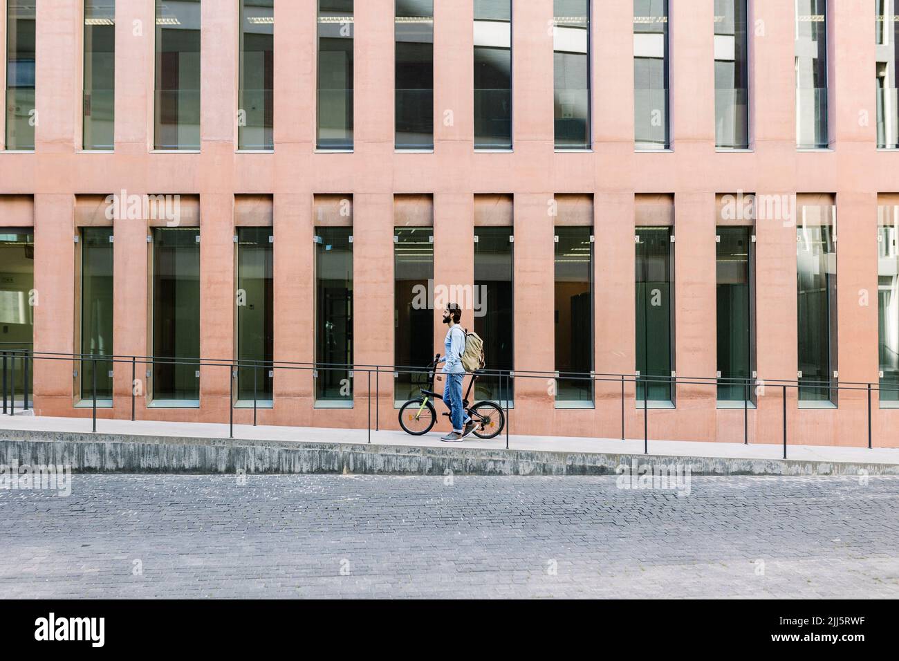 Man wheeling with bicycle by building Stock Photo - Alamy