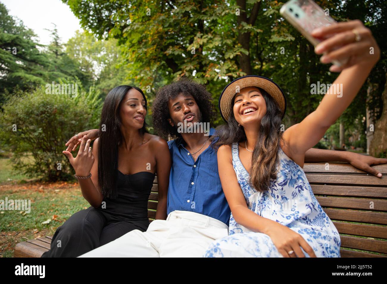 Three friends at the park take a selfie and smile happily, people of different ethnicities ...