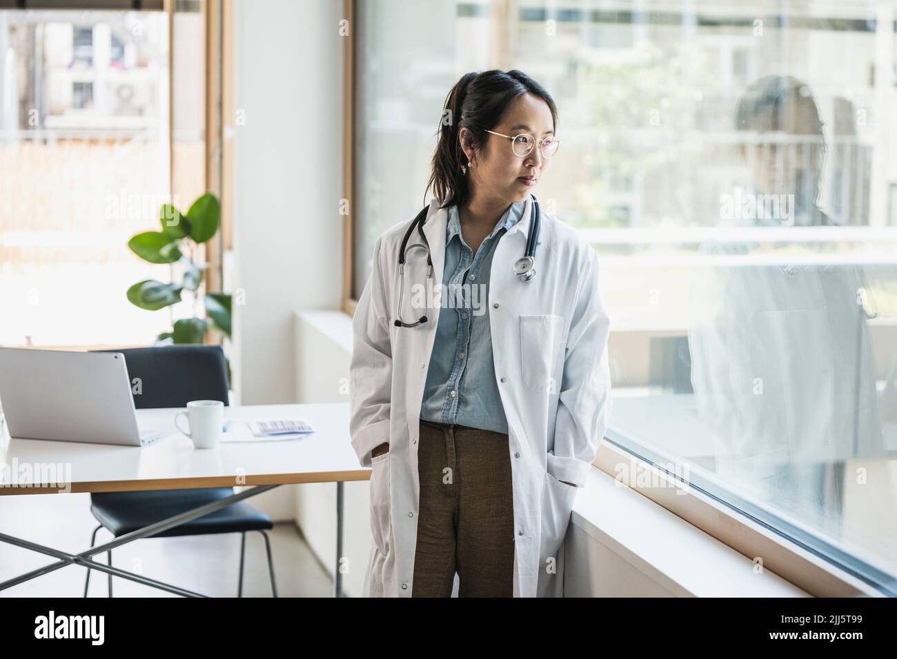 Female doctor standing by window in office Stock Photo - Alamy