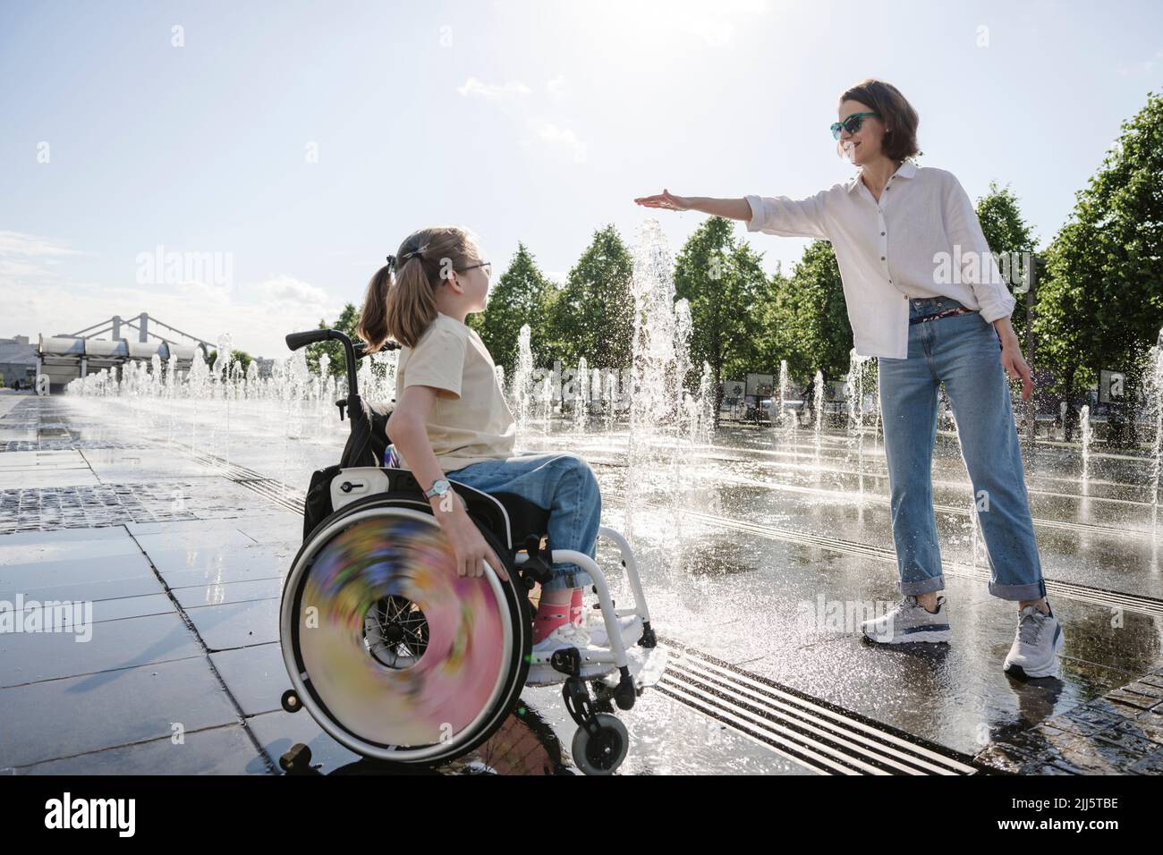 Girl with disability looking at mother playing with splashing fountain ...