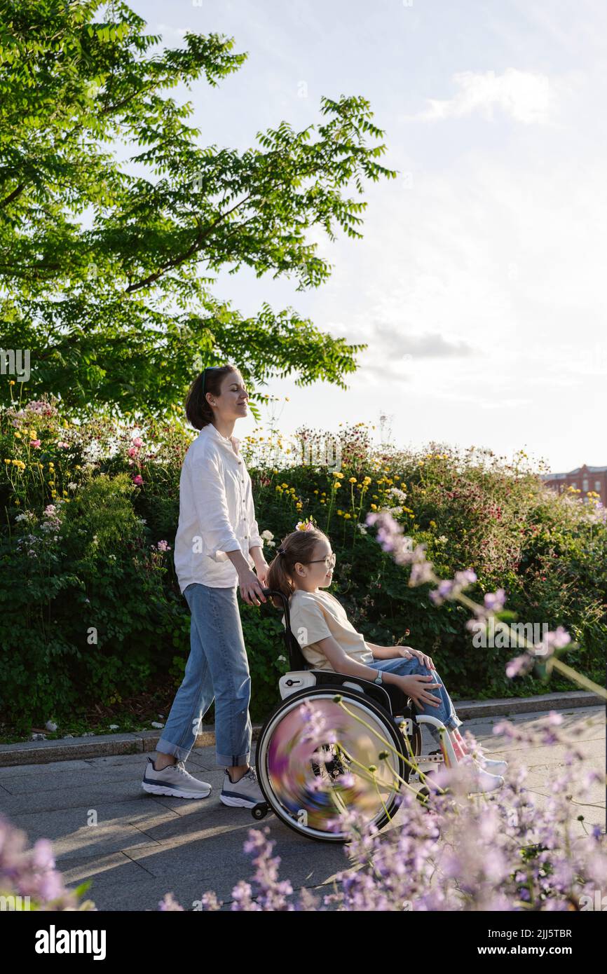 Woman pushing daughter with disability sitting in wheelchair at park ...