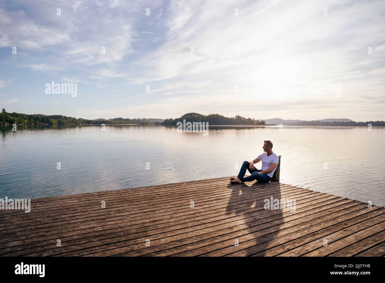Mature man sitting on pier by lake Stock Photo - Alamy